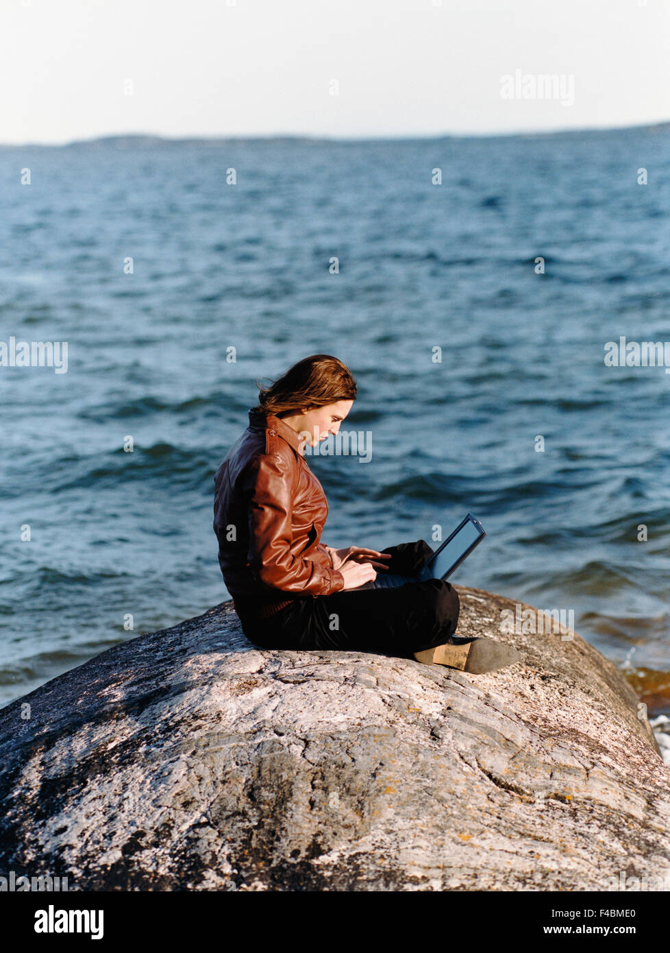 Woman sitting on rock by the sea with a computer in her lap Stock Photo ...