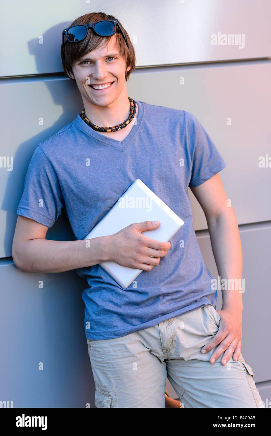 Smiling student boy leaning against modern wall Stock Photo - Alamy