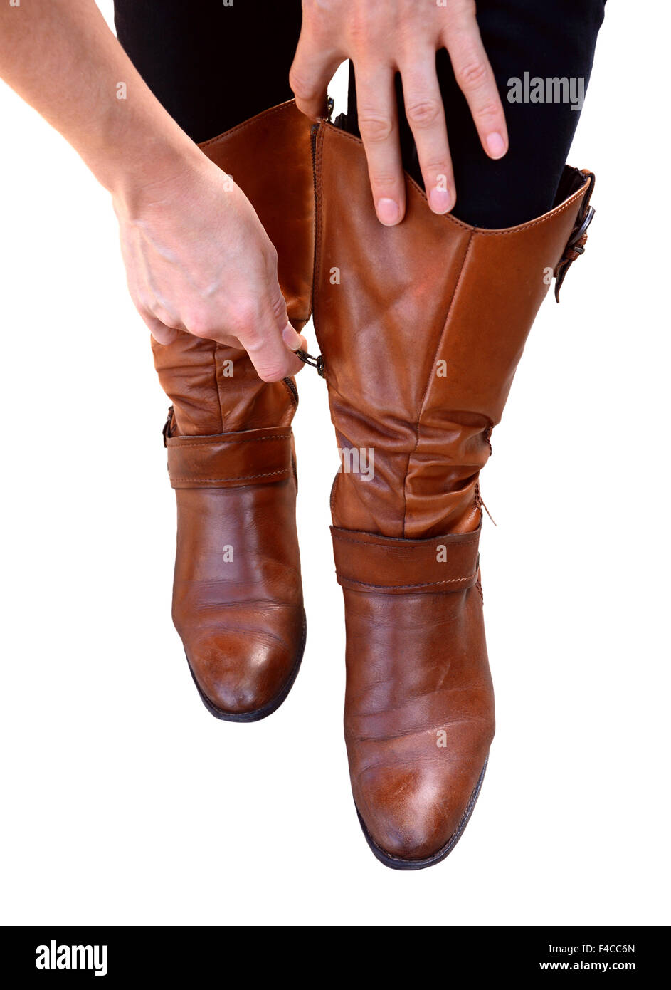 Woman holds her brown leather boots as she zips them up, isolated on a ...
