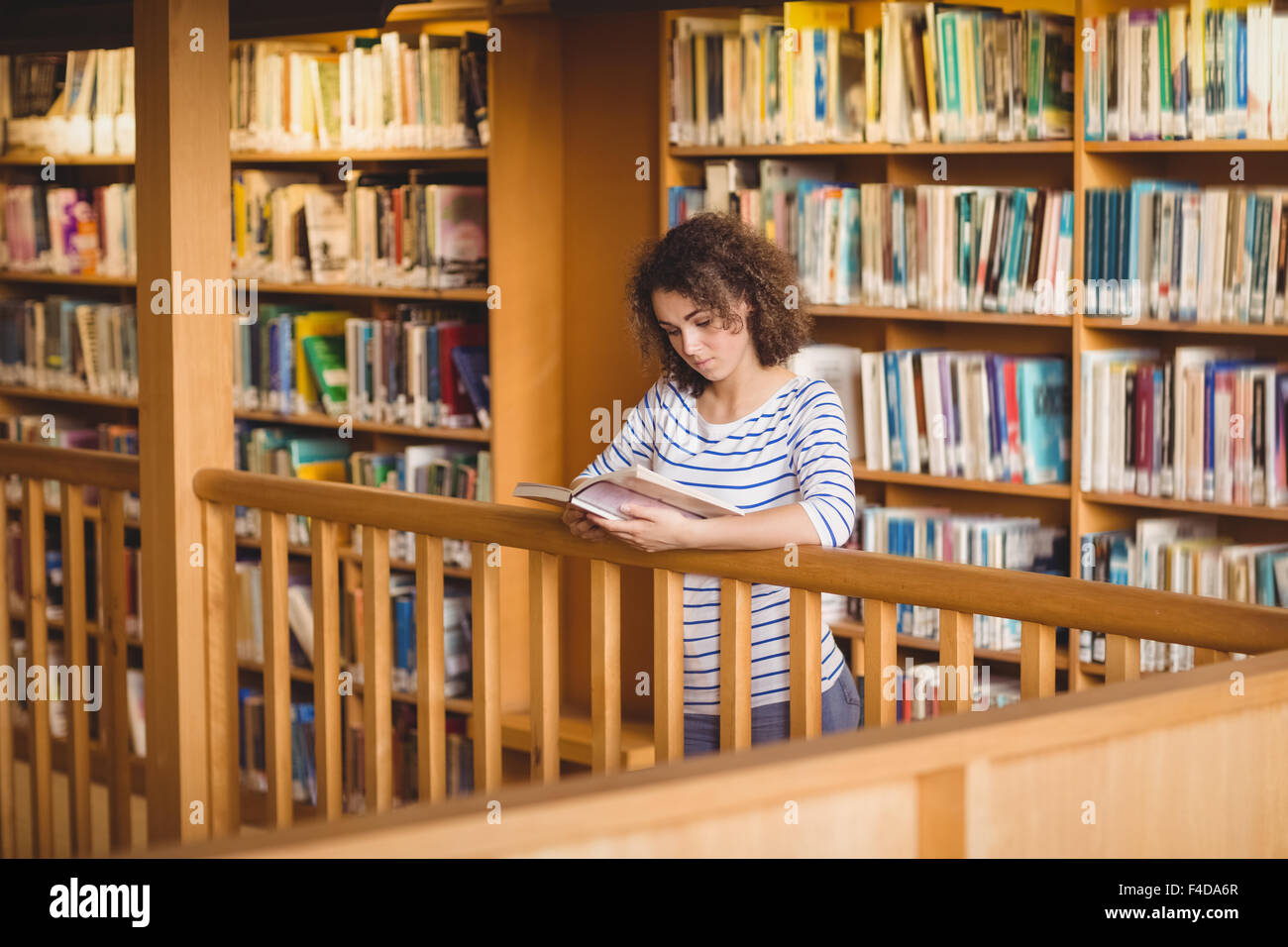 Pretty student in library reading book Stock Photo - Alamy