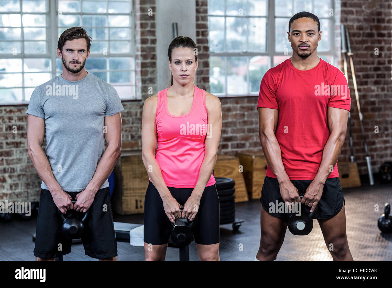 Three fit sporty people lifting kettlebell Stock Photo - Alamy