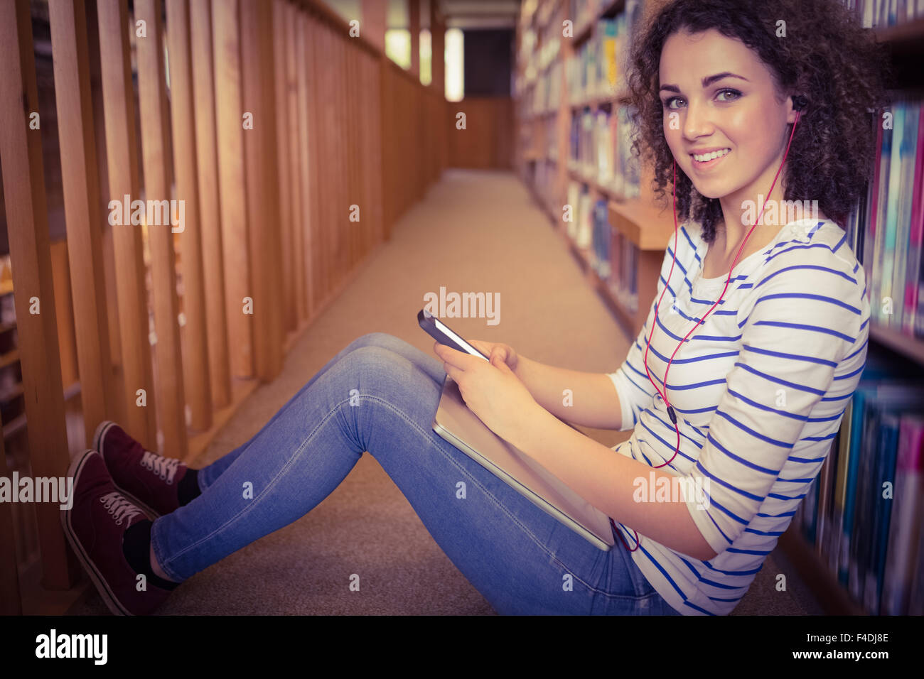 Pretty student in library sitting on the floor Stock Photo - Alamy