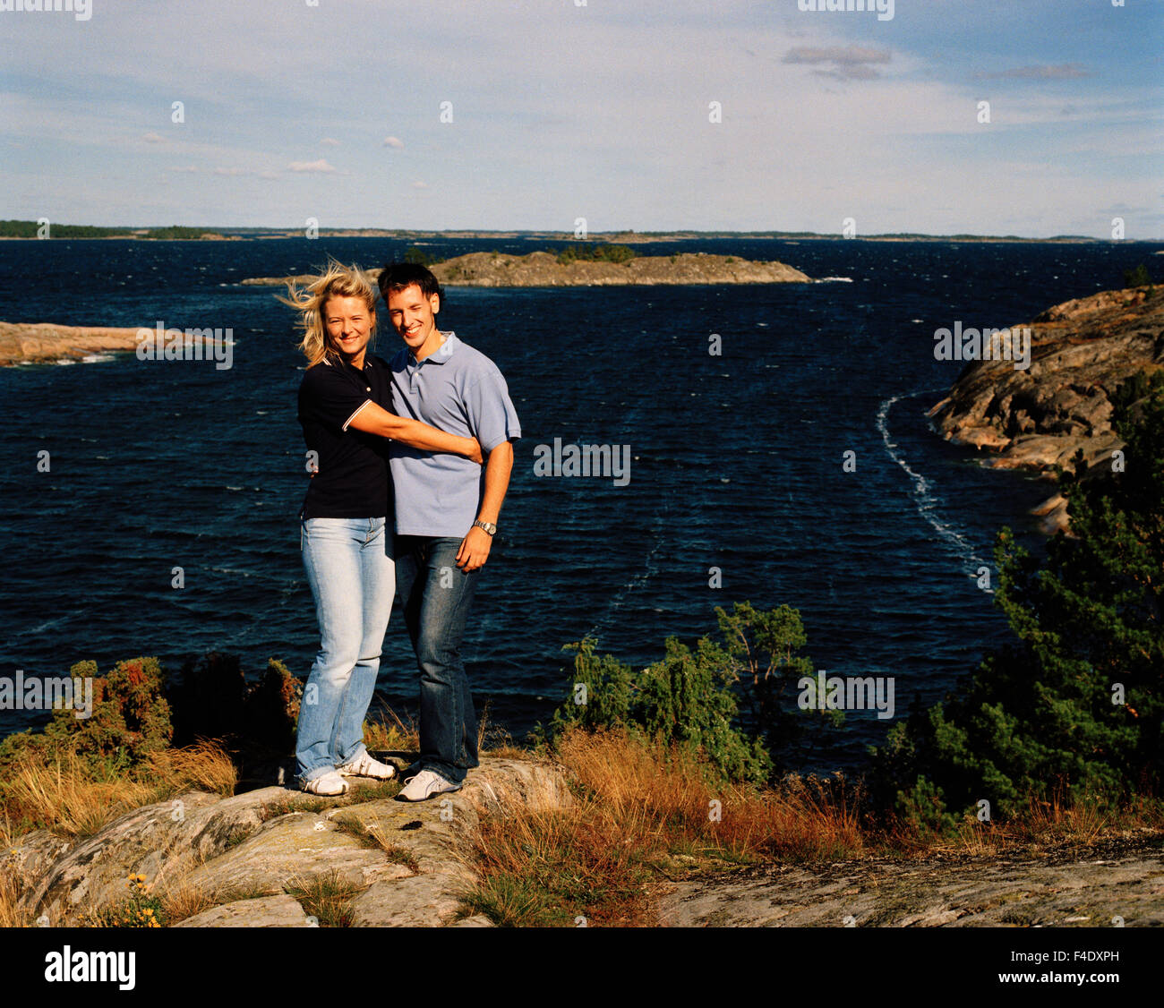 Young Scandinavian couple standing on rocks by sea, Harstena ...