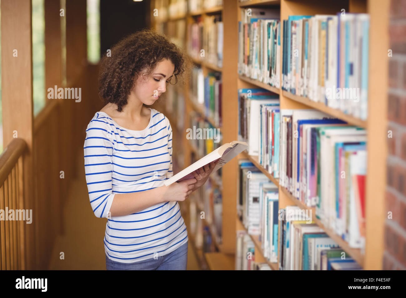 Pretty student in library reading book Stock Photo - Alamy