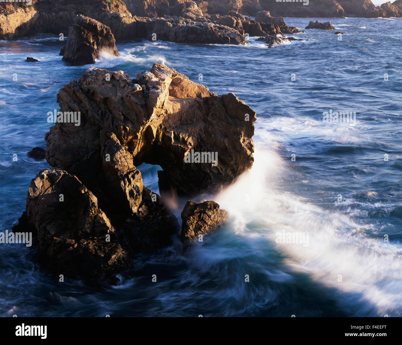 California, Big Sur Coast, A wave crashes against an arch sea stack on ...