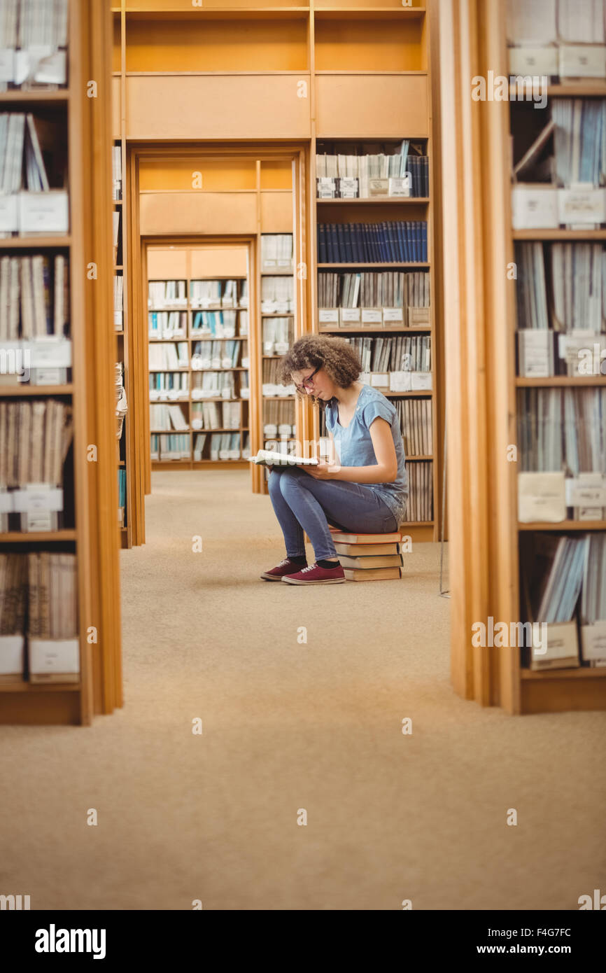 Pretty student in library sitting on books Stock Photo - Alamy