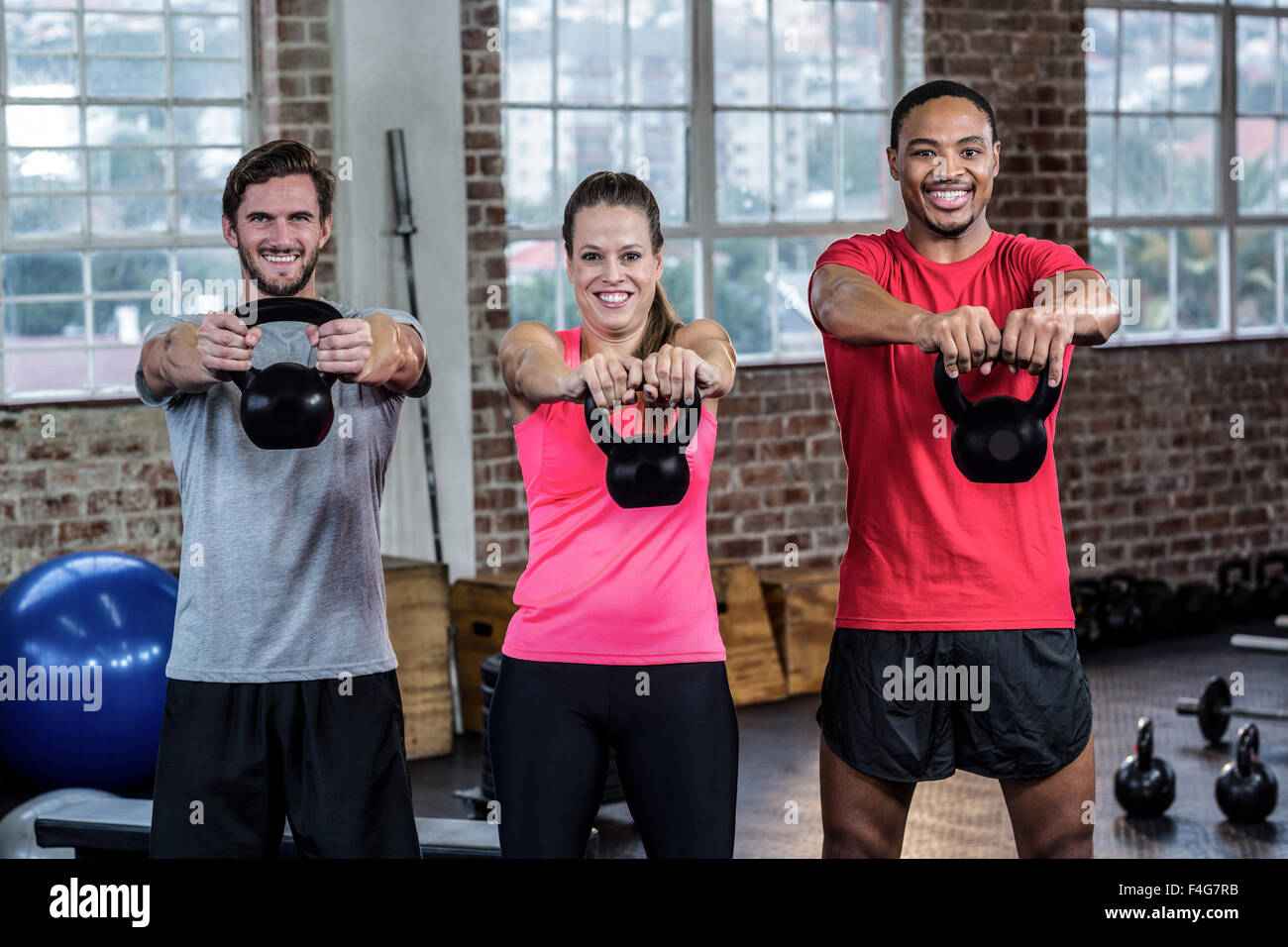 Three fit sporty people lifting kettlebell Stock Photo - Alamy