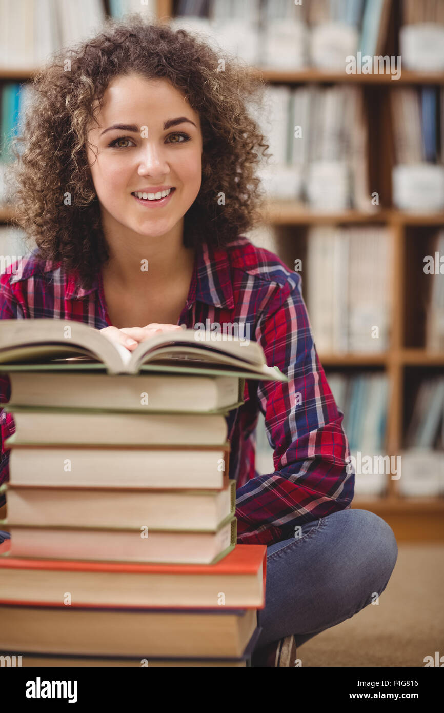 Pretty student in library with pile of books Stock Photo - Alamy