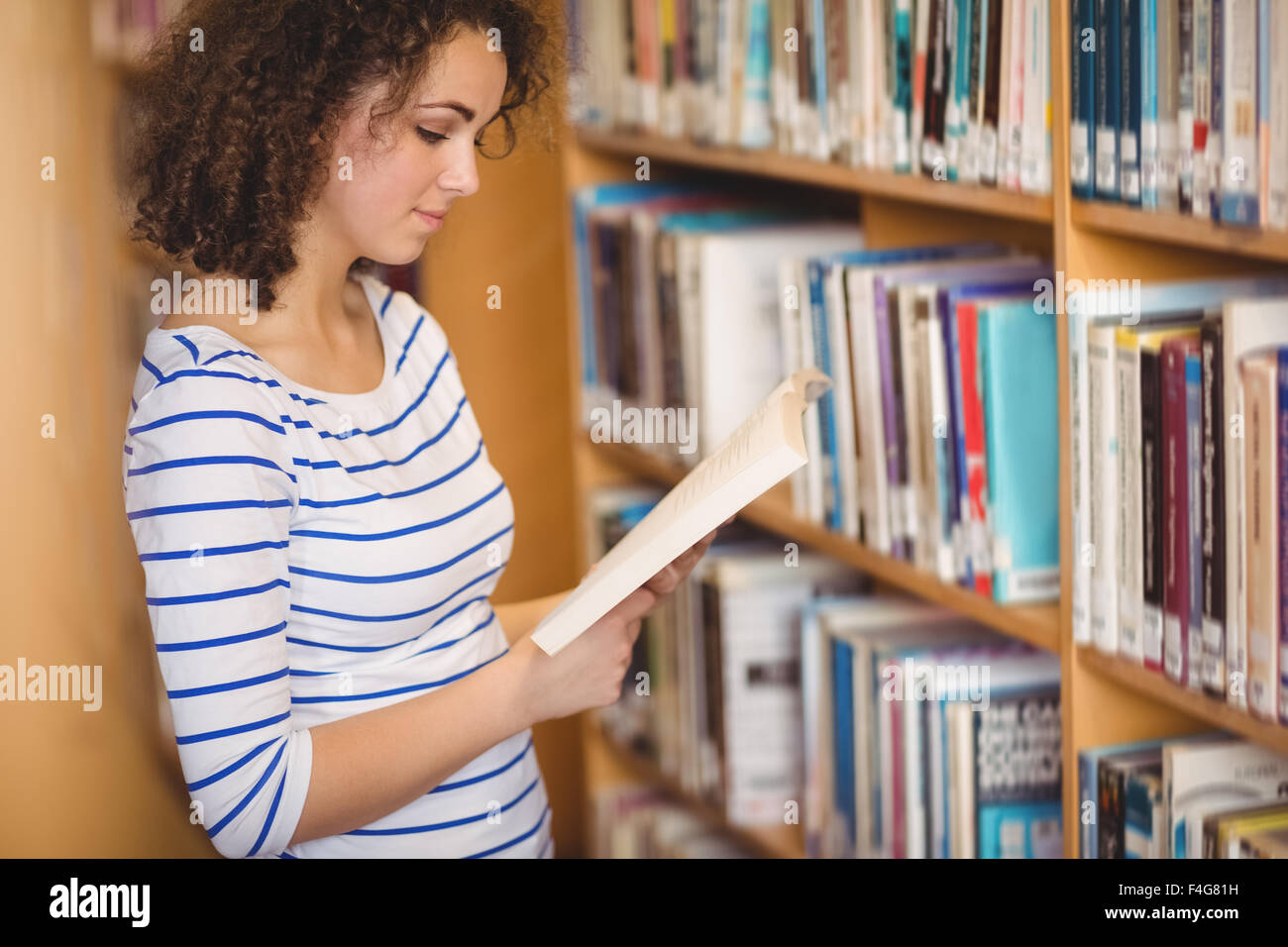 Pretty student in library reading book Stock Photo - Alamy