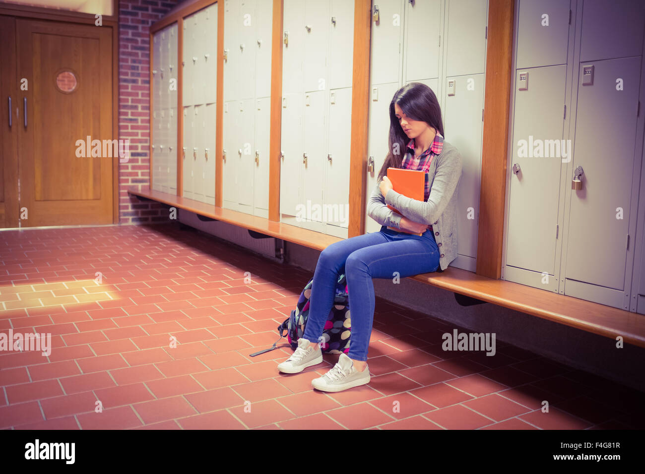 Worried student holding book while sitting on bench Stock Photo - Alamy