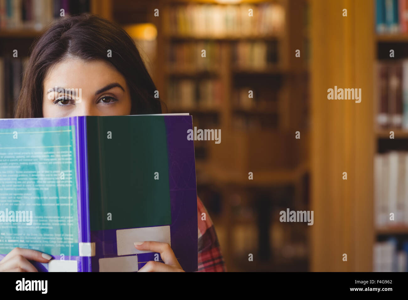 Close-up portrait of female student peeking over book Stock Photo - Alamy