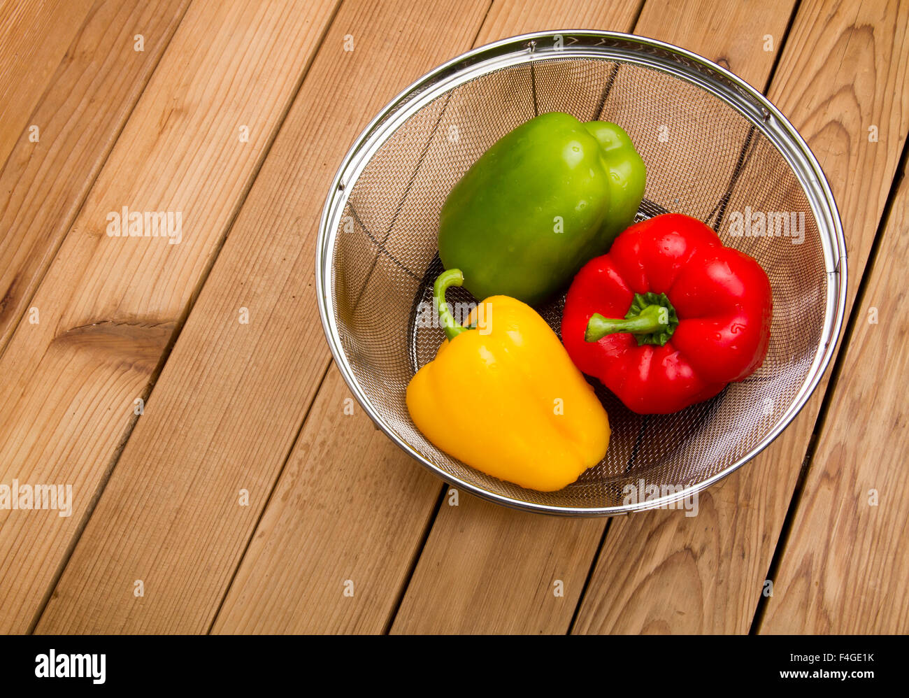 Three Bell peppers sitting on a wooded table in a kitchen strainer ...