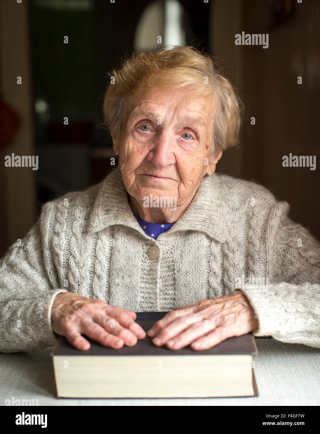 Old woman sitting at a table with a book Stock Photo - Alamy