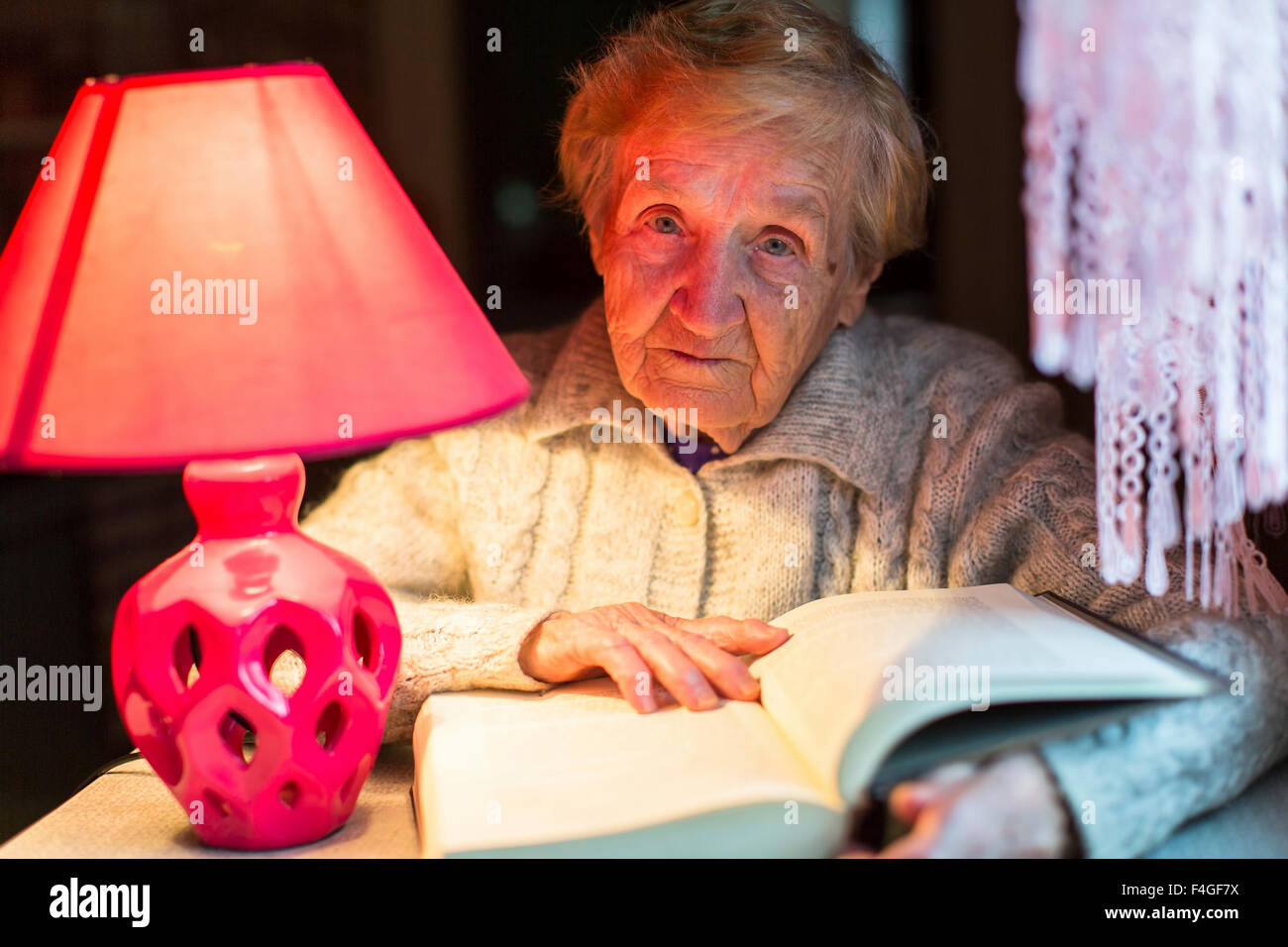 Elderly woman reading a book sitting at a table with a lamp Stock Photo ...