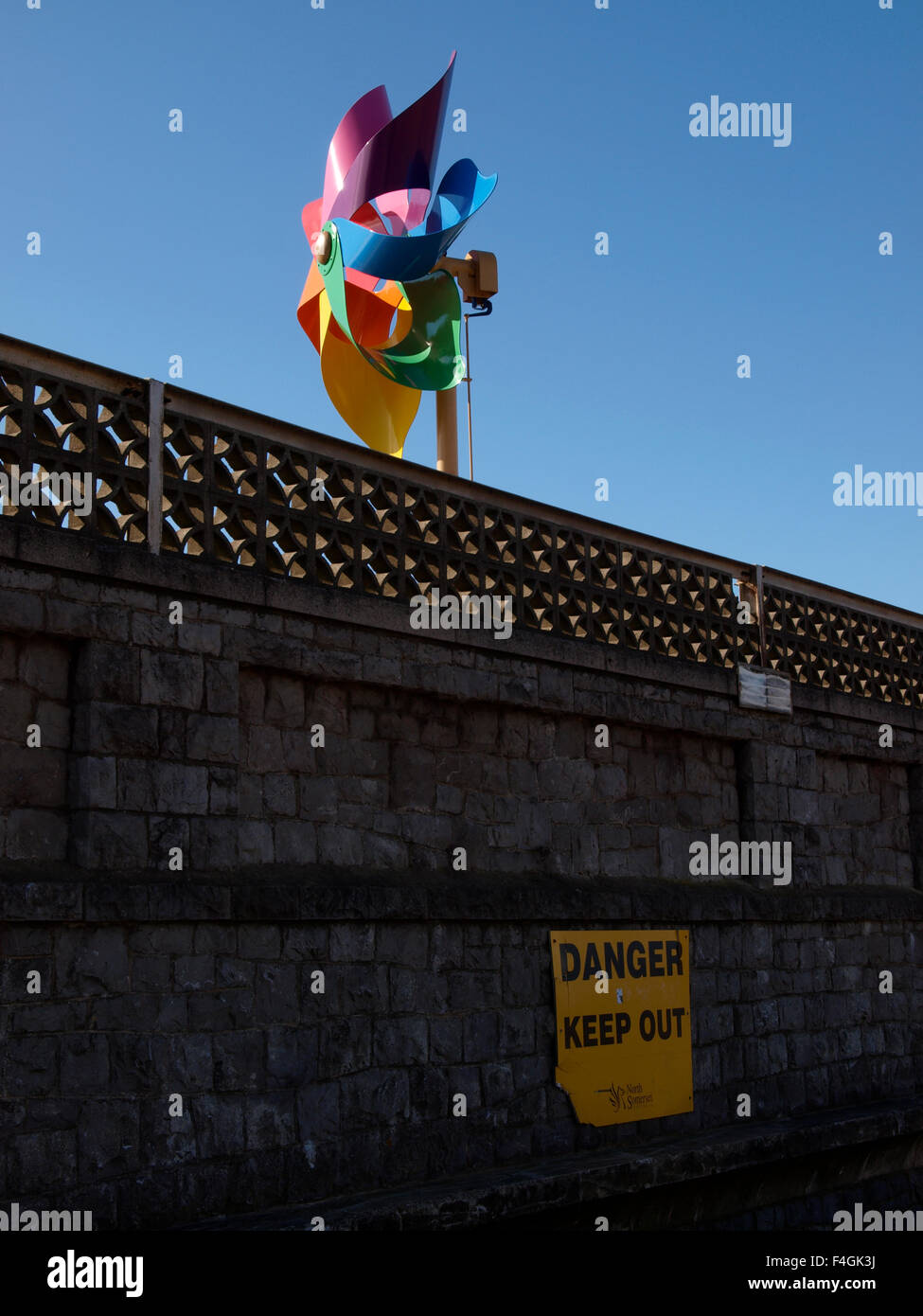 Danger keep out sign on a wall with a giant children's windmill behind ...