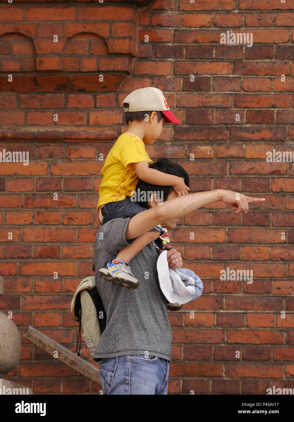 A small chinese boy sitting on his dad's shoulders while the dad points ...