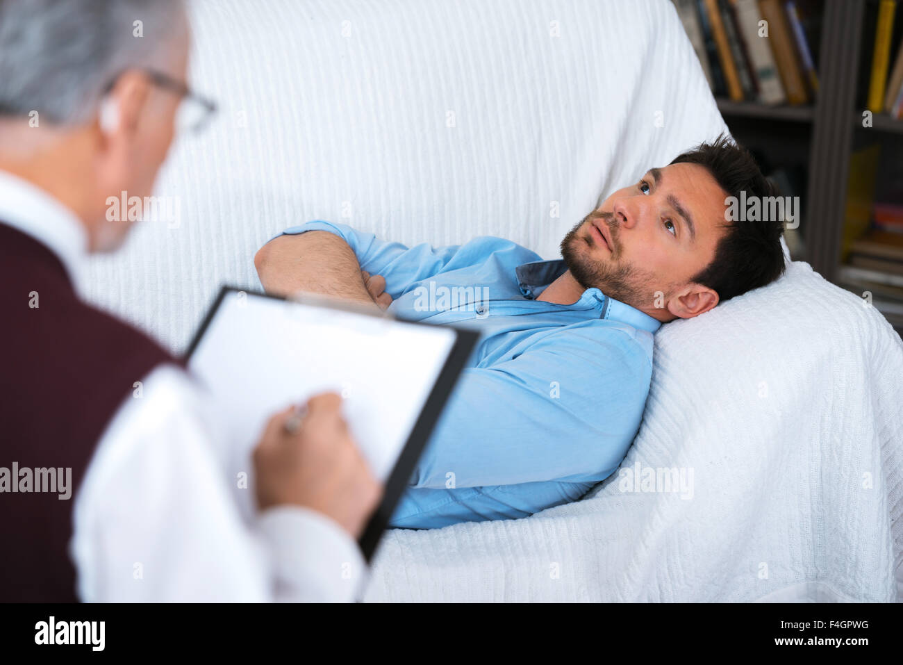 Sad young man talking with psychologist and lying on coach ...