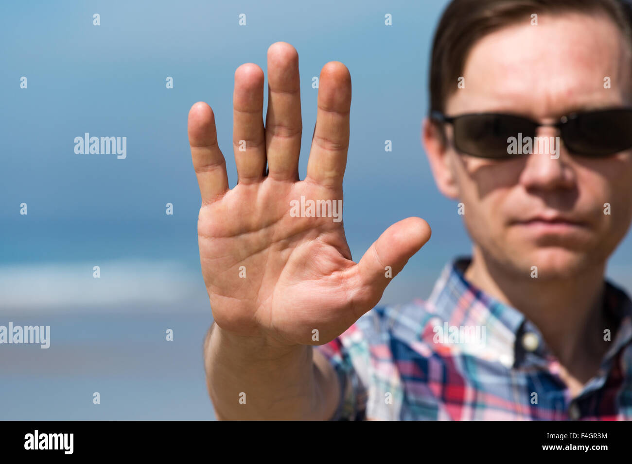 Man in Sunglasses Showing Stop Sign with his Hand, blue sky background ...