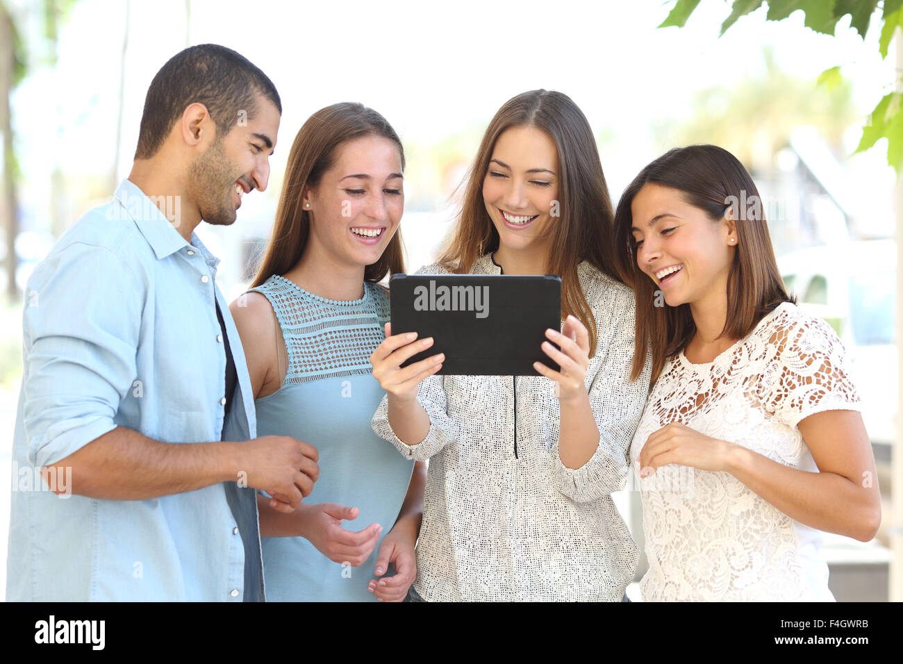 Front view of a group of four happy friends watching videos on a tablet ...