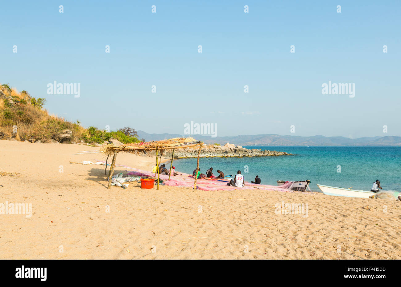 Local fishermen mending their fishing nets on the sunny lakeside beach ...