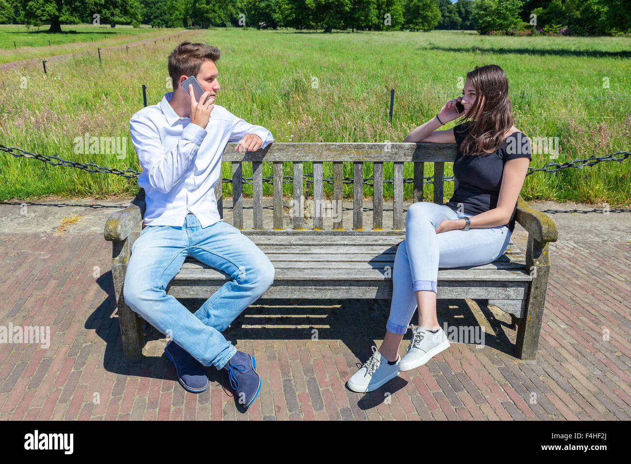 Young attractive caucasian couple on bench calling each other with ...
