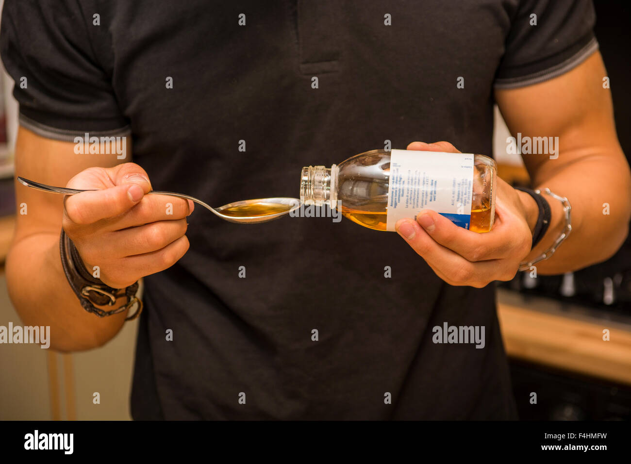 Sick young man pouring cough syrup or medication in spoon, in home ...