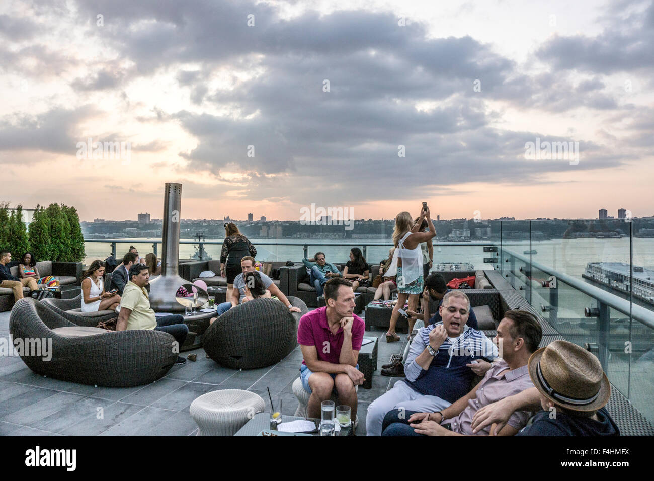 relaxed people enjoy drinks socializing & sunset view of Hudson river ...