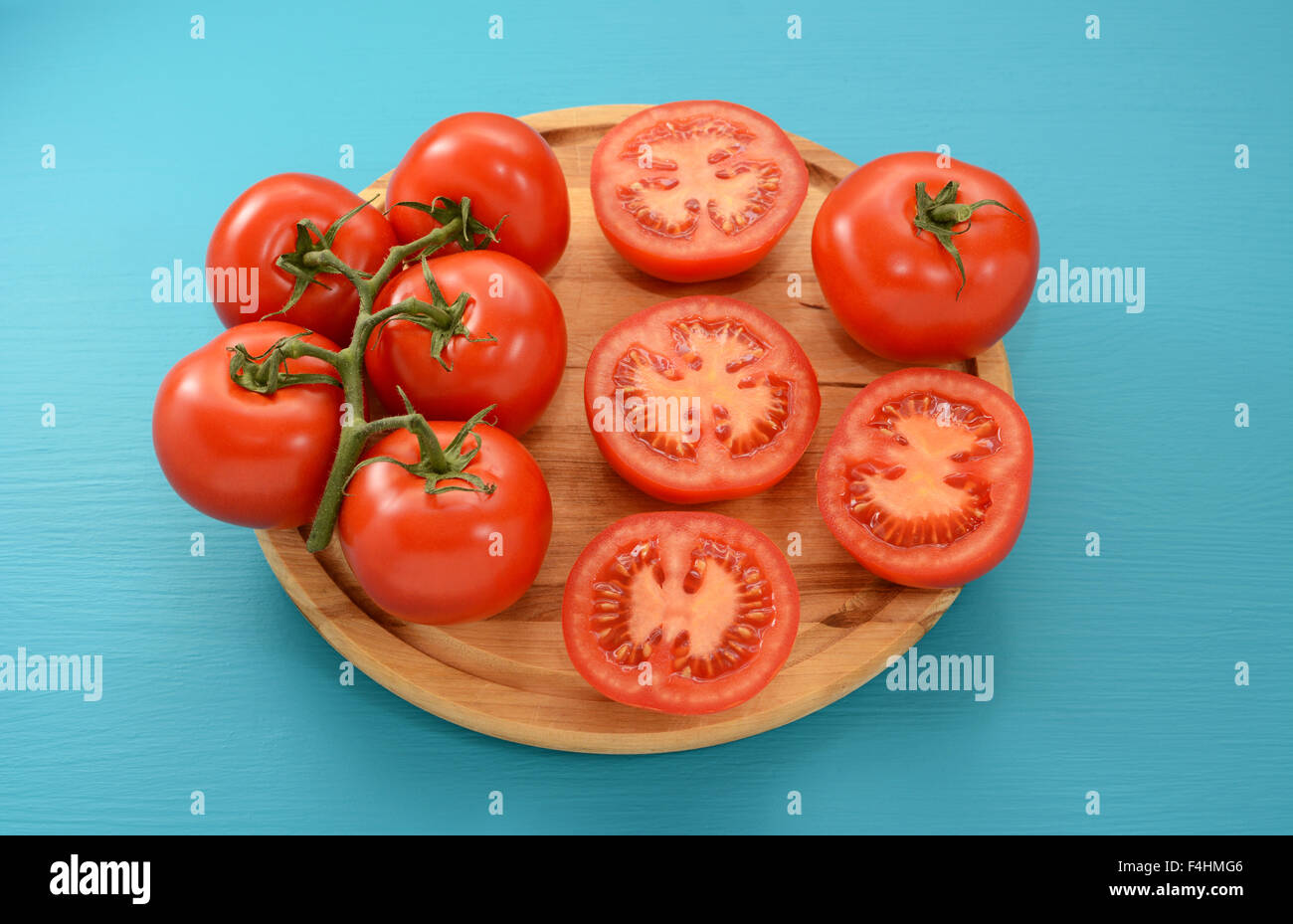 Fresh tomatoes - on the vine, halved and whole on a circular wooden ...
