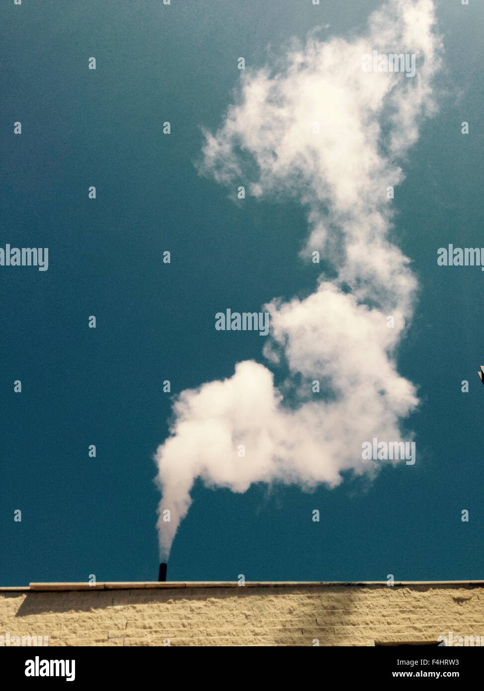 Industrial laundry smokestack spewing white steam cloud vertically up ...