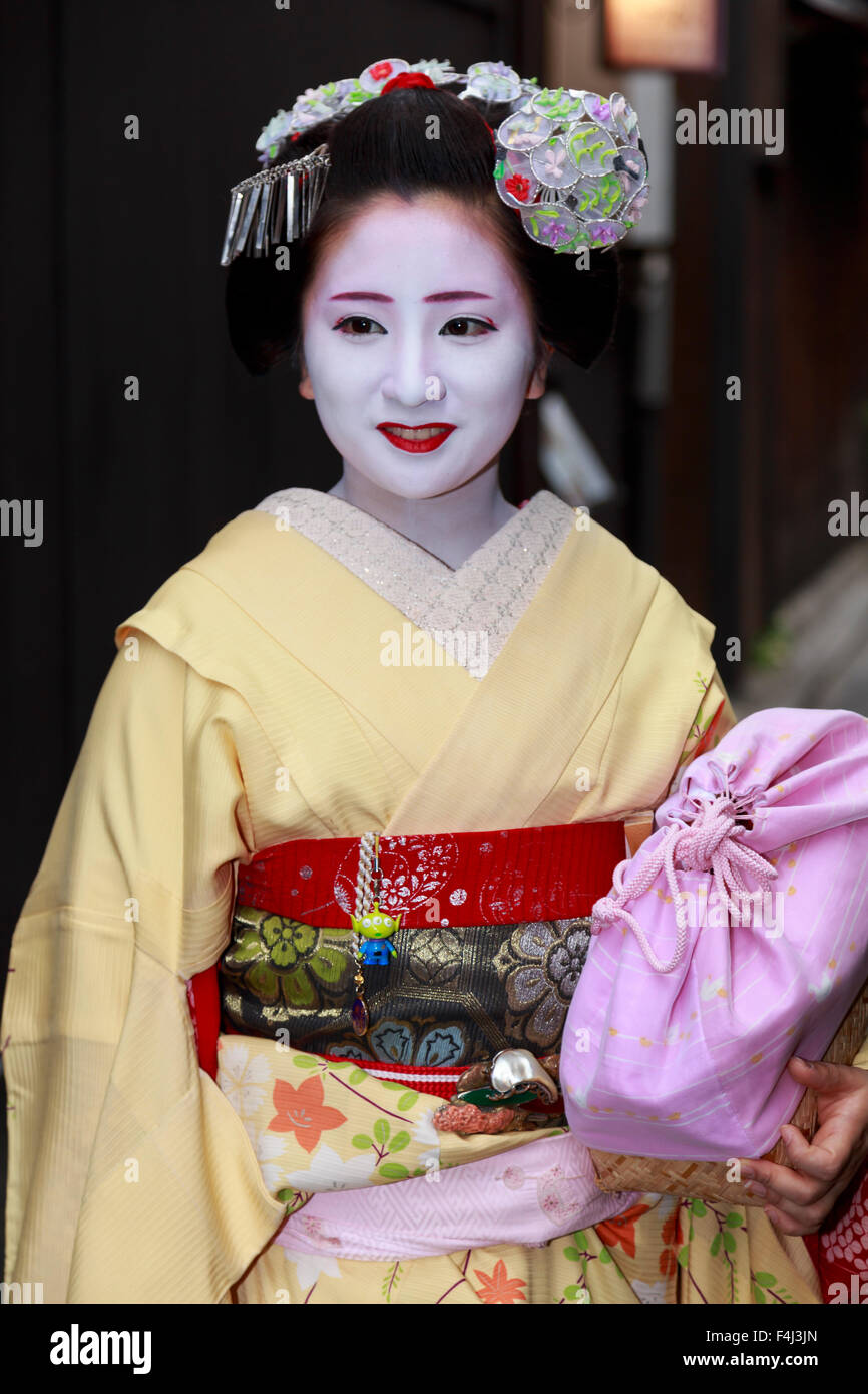 Smiling maiko, apprentice geisha, with yellow robes, stops in street on ...