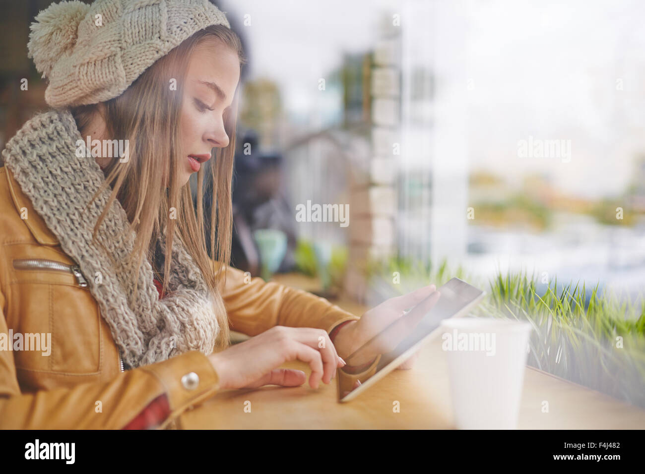 Cute girl in knitted cap and scarf using touchpad Stock Photo - Alamy