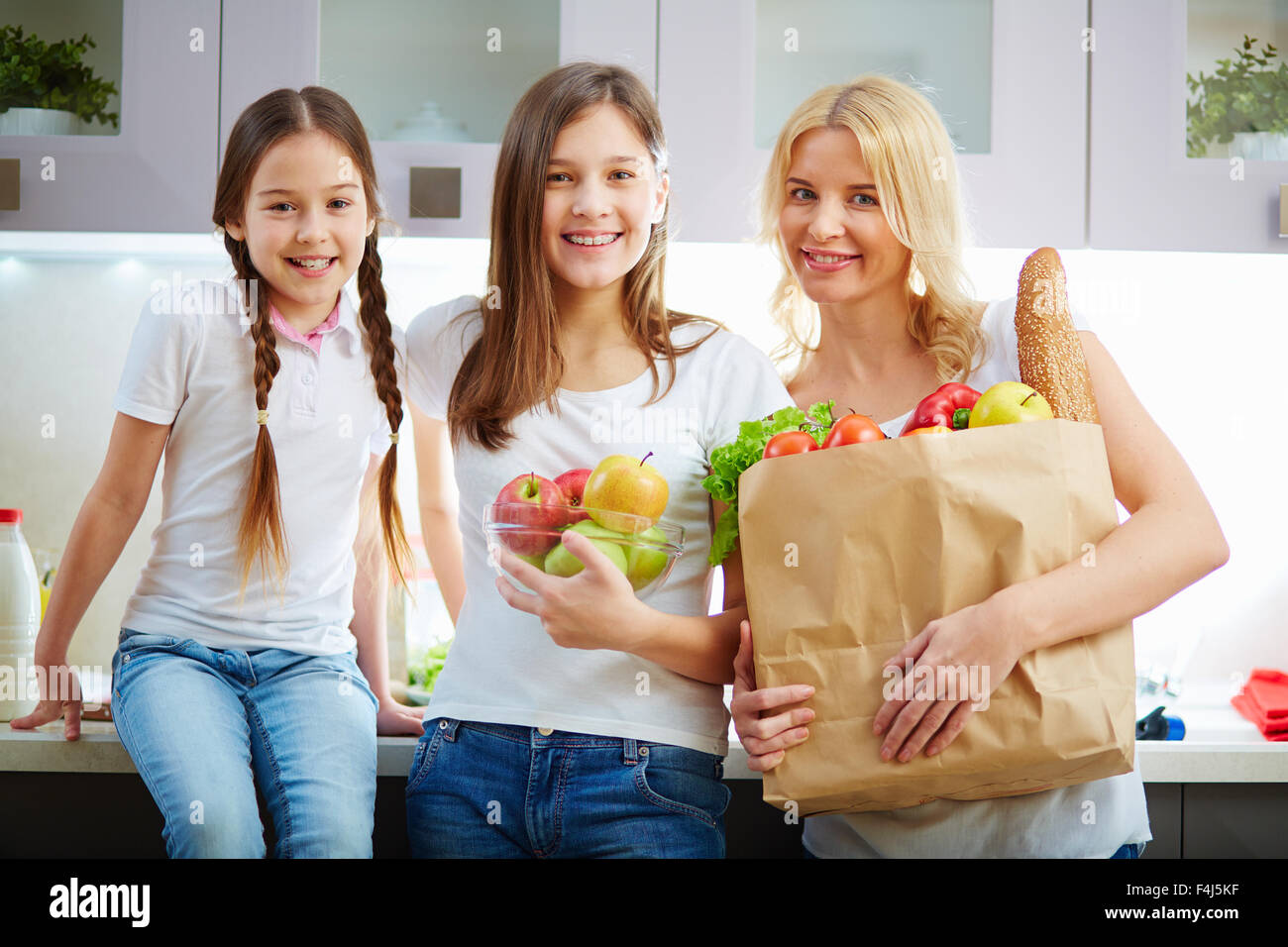 Young woman and two adolescent girls looking at camera in the kitchen ...