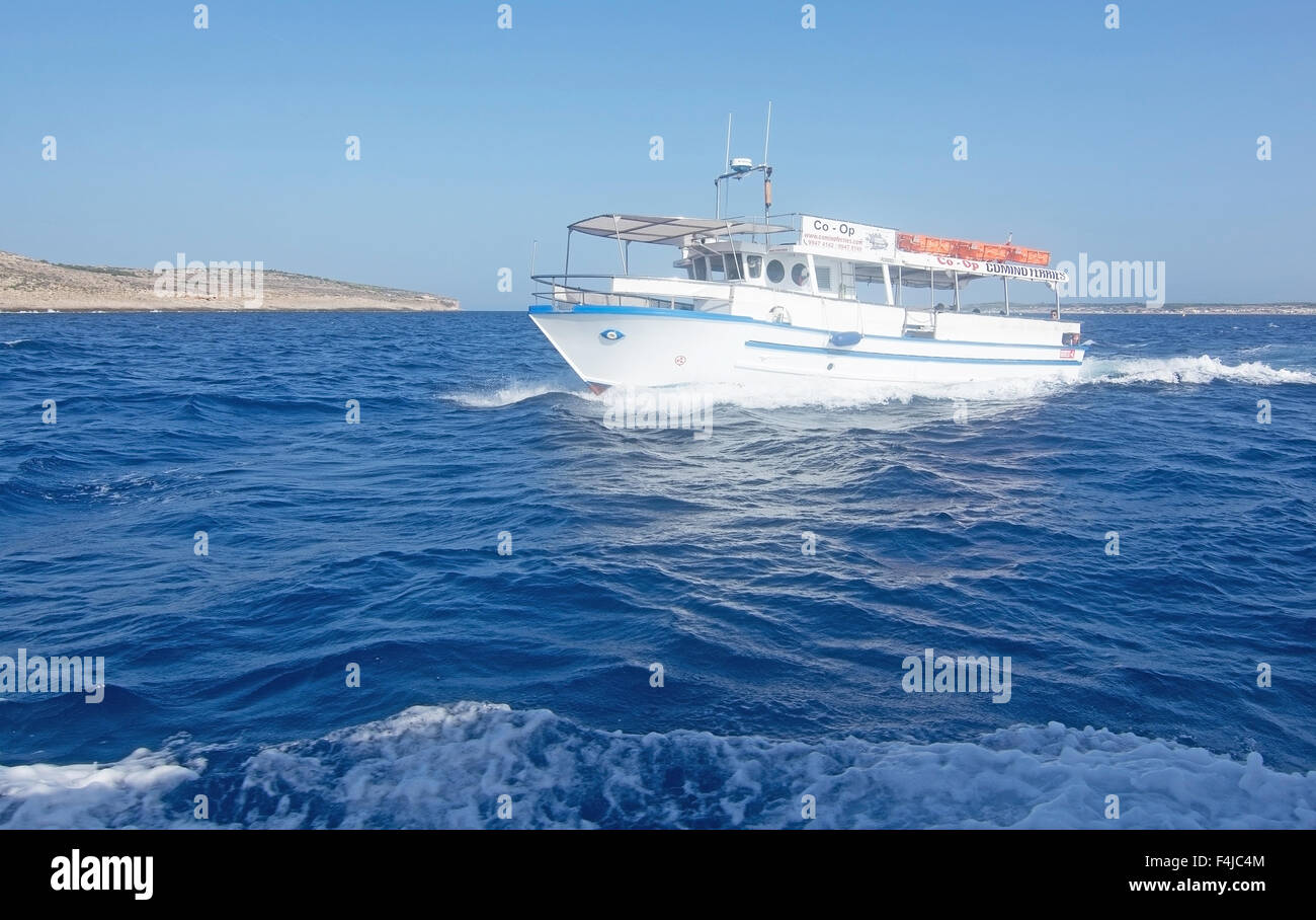 Small white ferry boat from the co-op Comino Ferries passes by fort on ...