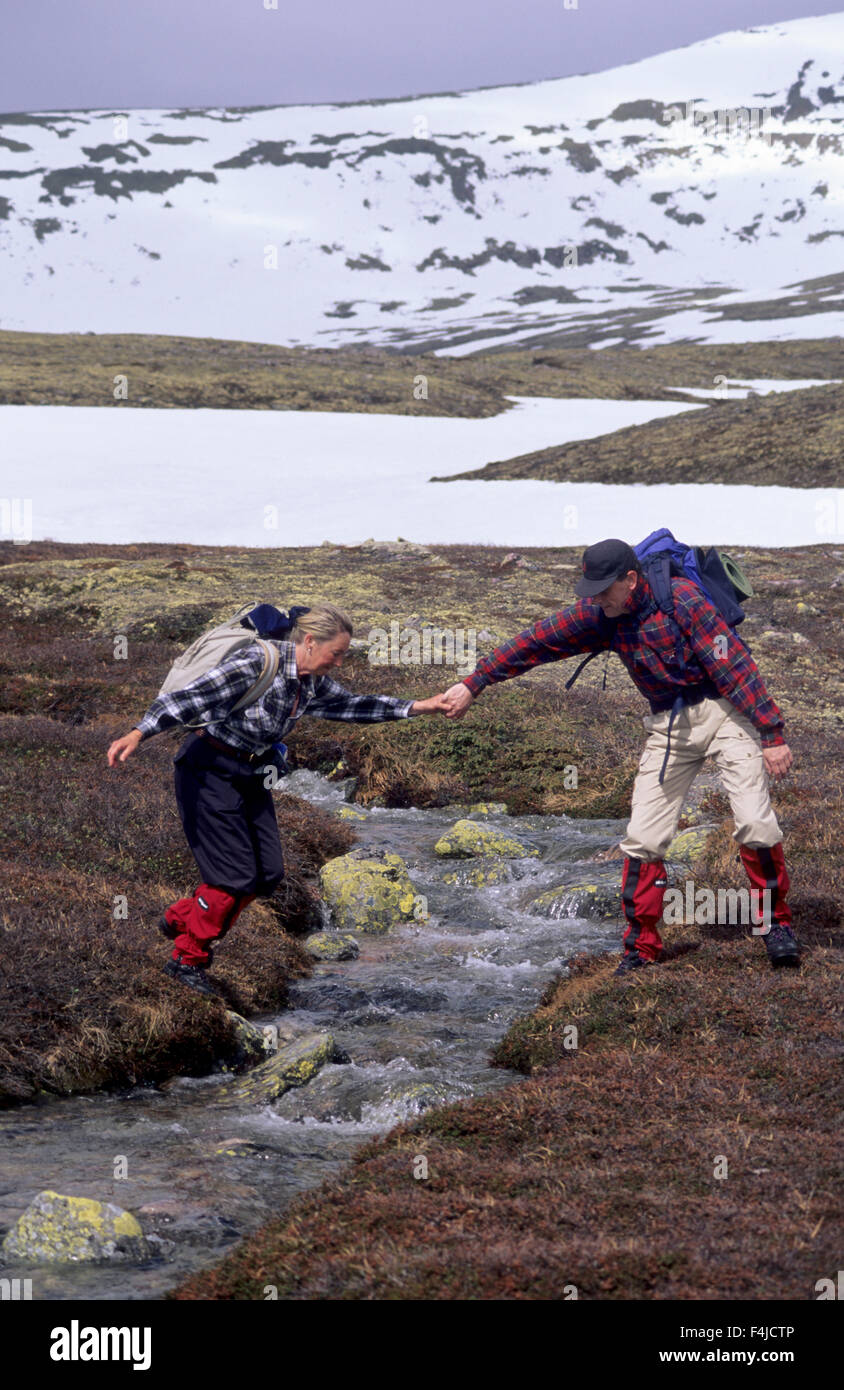Scandinavia, Sweden, Dalarna, Man helping woman while crossing stream ...