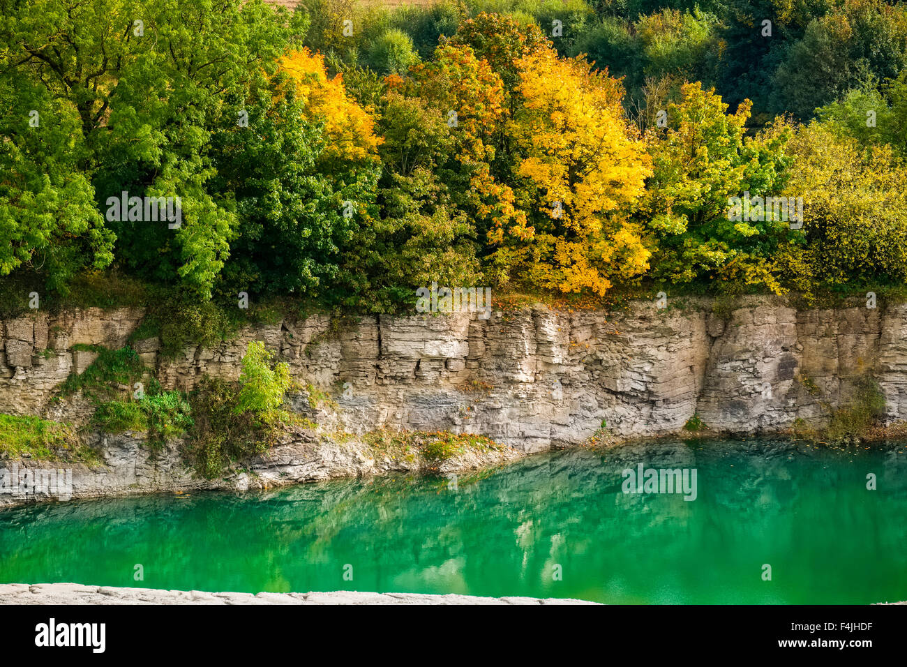 Autumn trees along a limestone cliff above the lagoon at Lea Quarry on ...