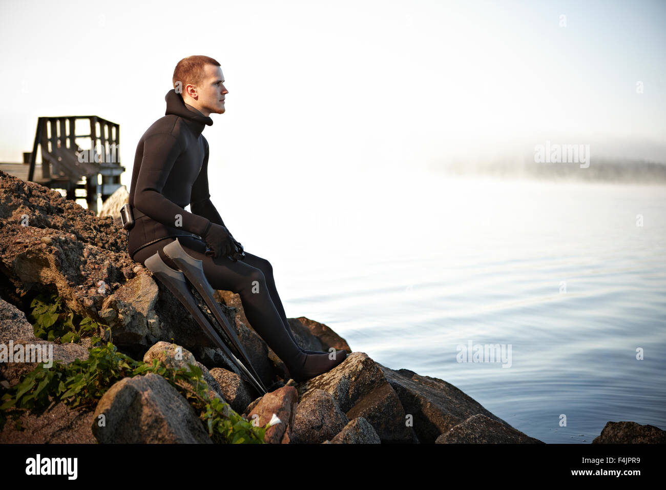 Man in diving suit sitting on rock, side view Stock Photo - Alamy