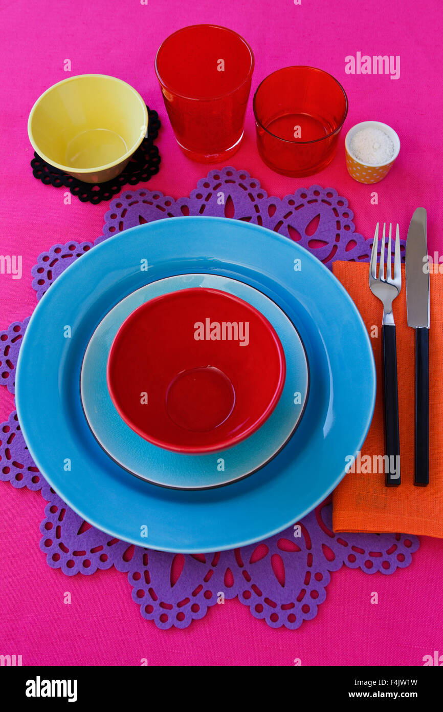 Multi colored crockery and cutlery on pink surface Stock Photo - Alamy