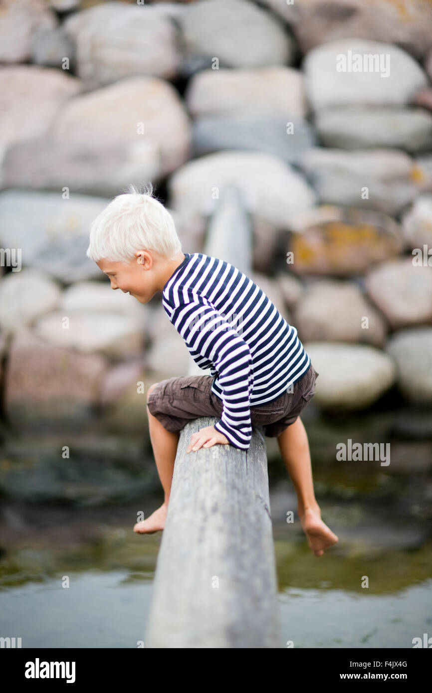 Boy sitting on log over stream Stock Photo - Alamy