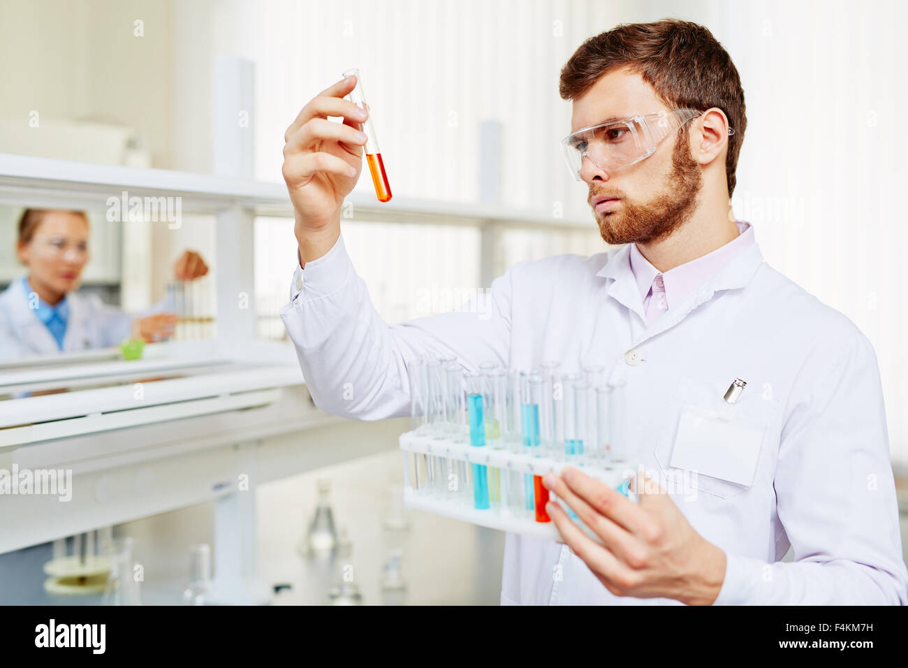 Young chemist analyzing new substance in lab on background of his ...