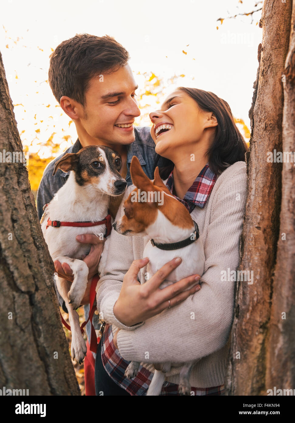 Happy romantic young couple with two dogs in autumn park between trees ...