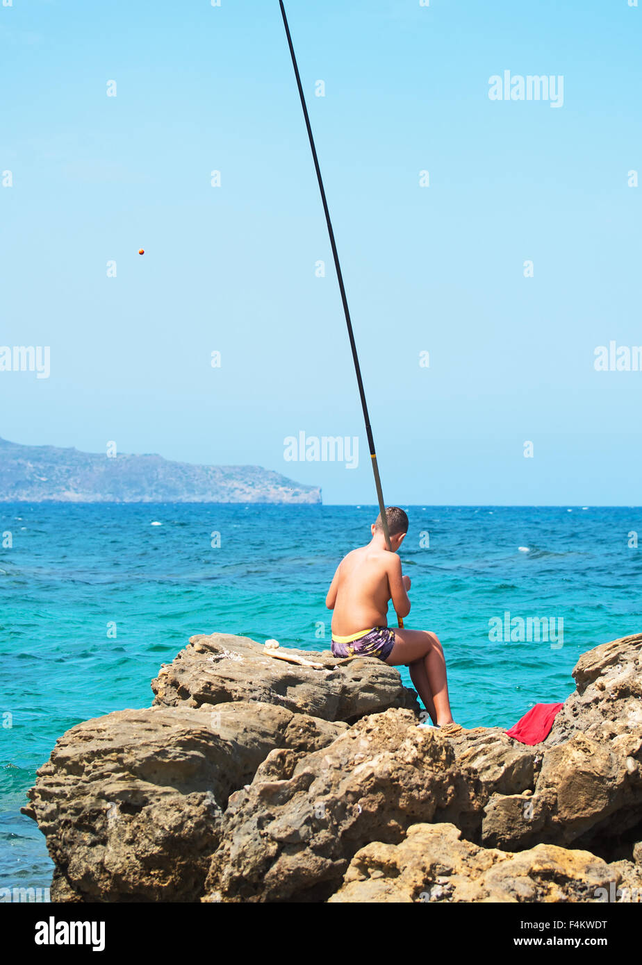 Boy fishing on rocks by the sea Stock Photo - Alamy