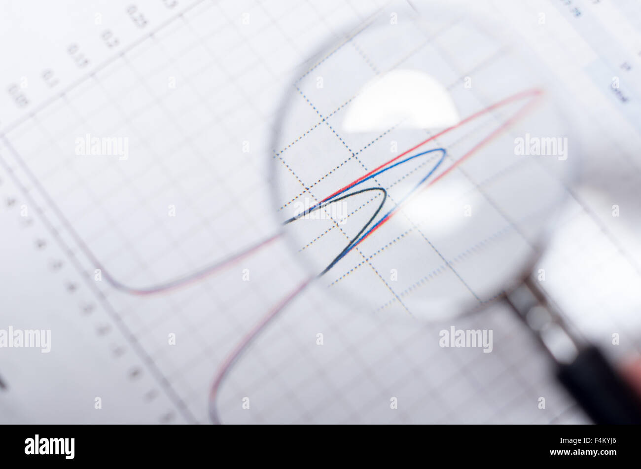 Closeup magnifying glass over paper with red and blue graph visible ...
