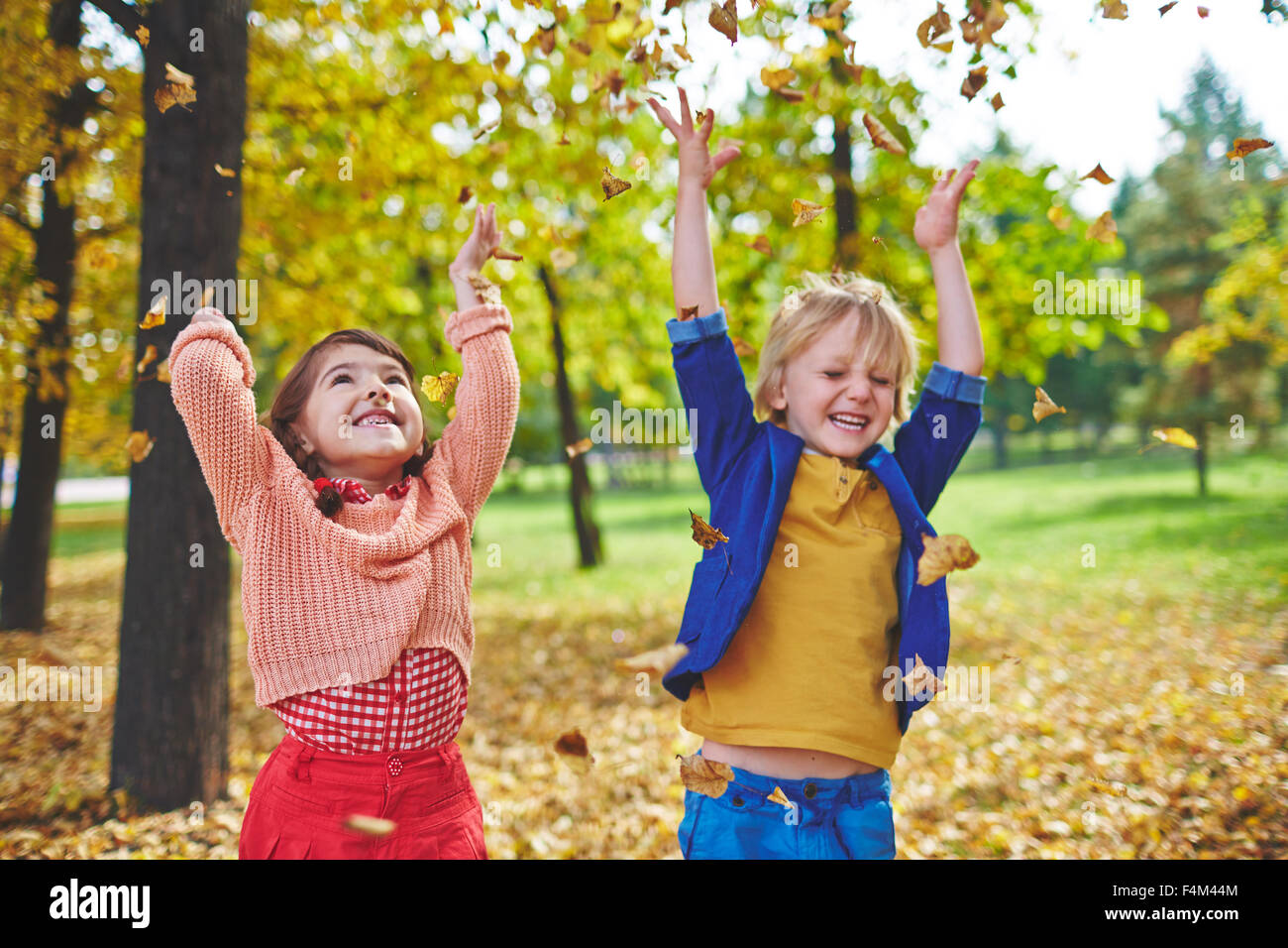 Ecstatic little friends playing with falling leaves in park Stock Photo ...