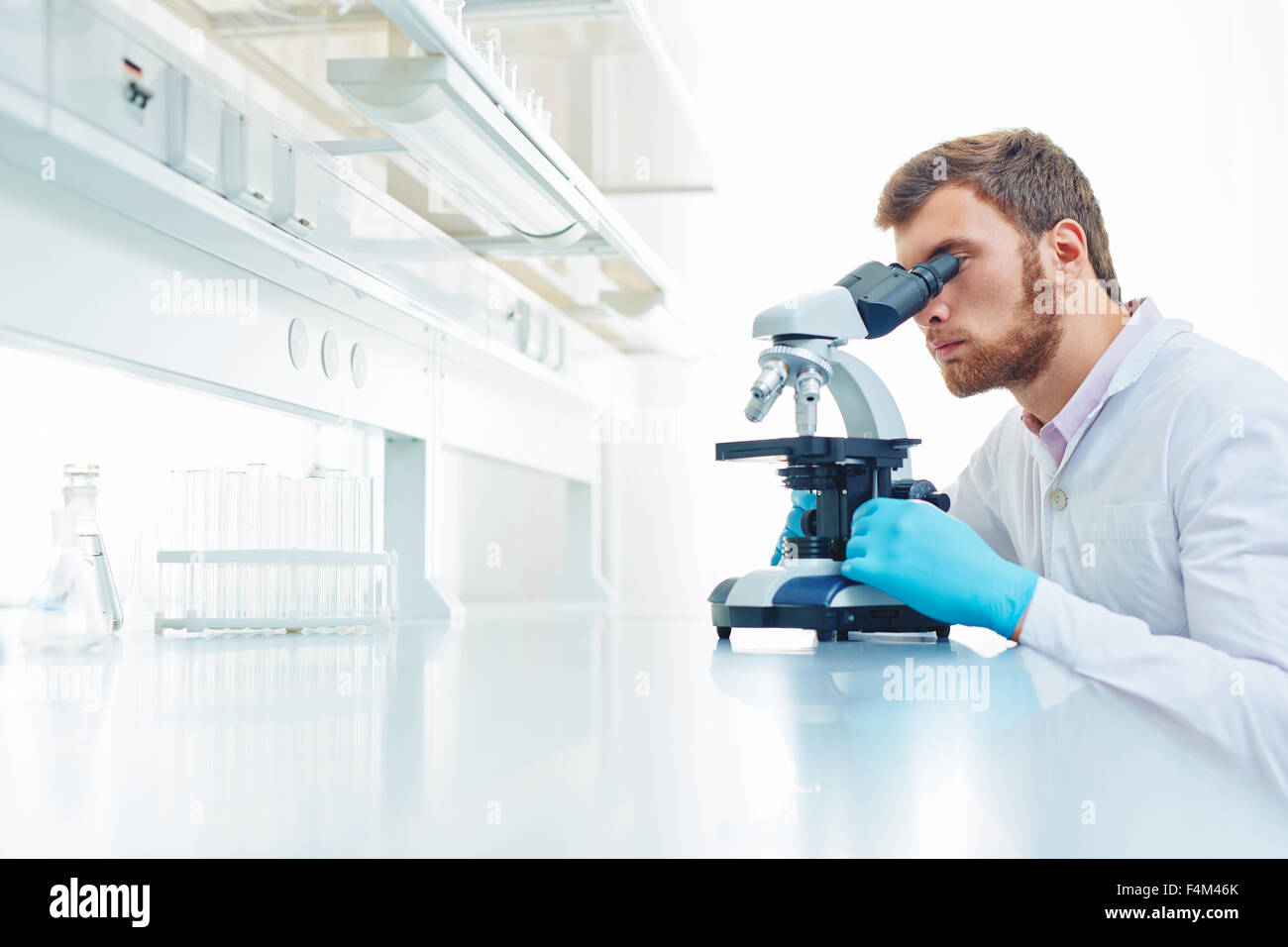 Young scientist investigating microbiological substance in microscope ...