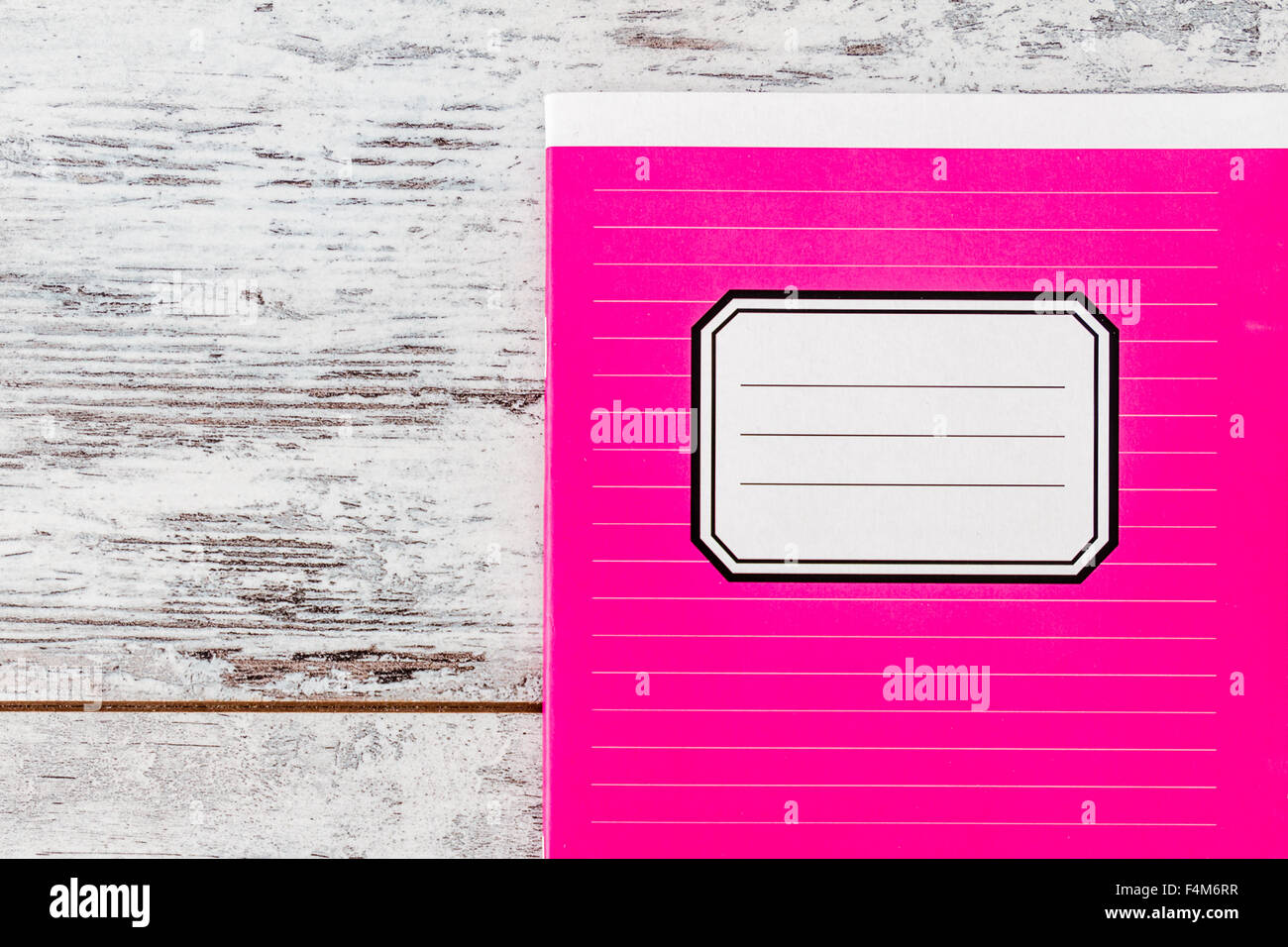 Pink notebook with name label on cover on white wooden background, copy ...
