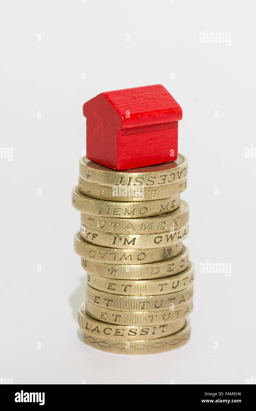 Stack of British one pound coins with a wooden Monopoly-style house ...