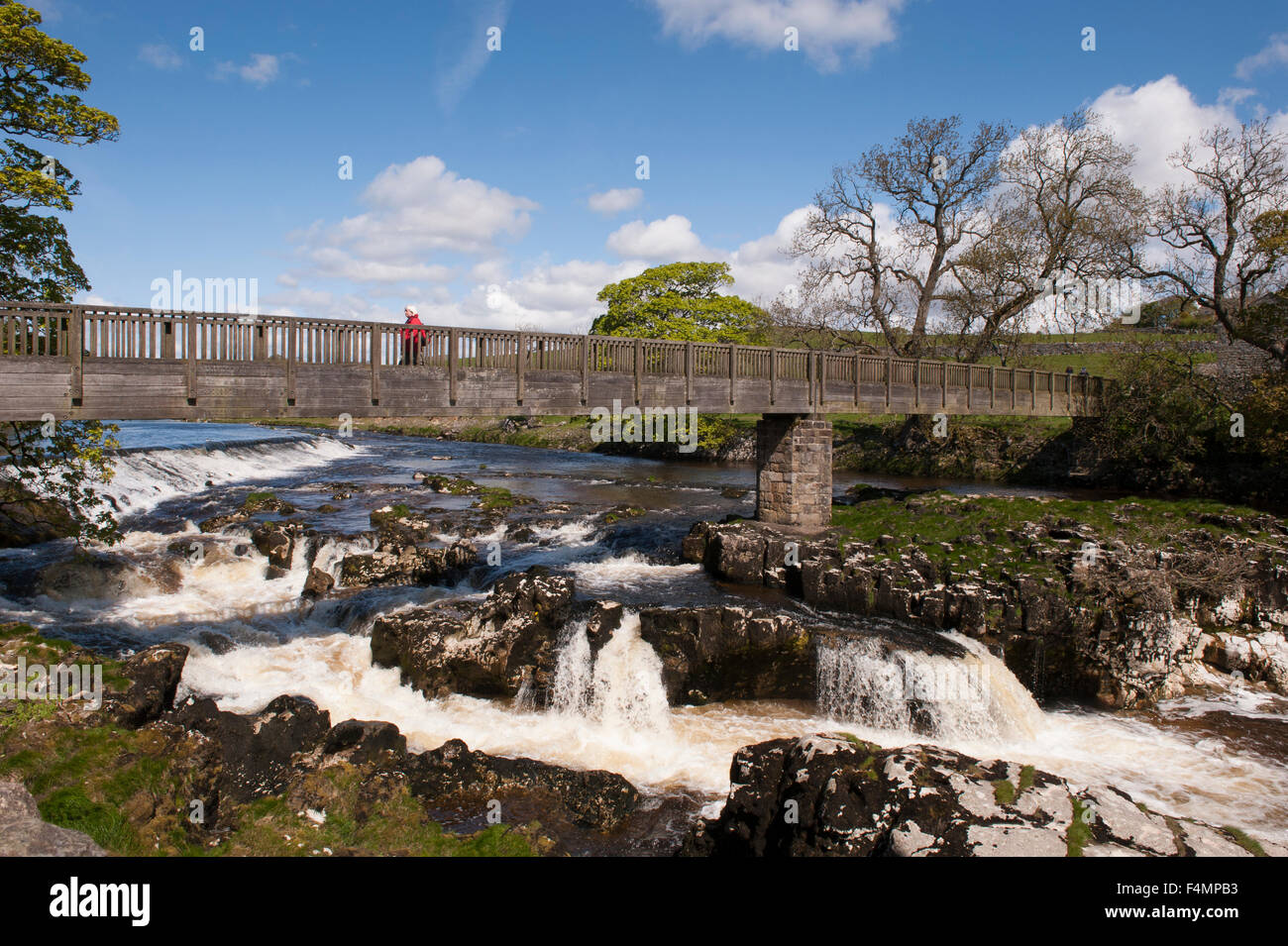 Sunny day with blue sky, lady is crossing wooden footbridge over scenic ...