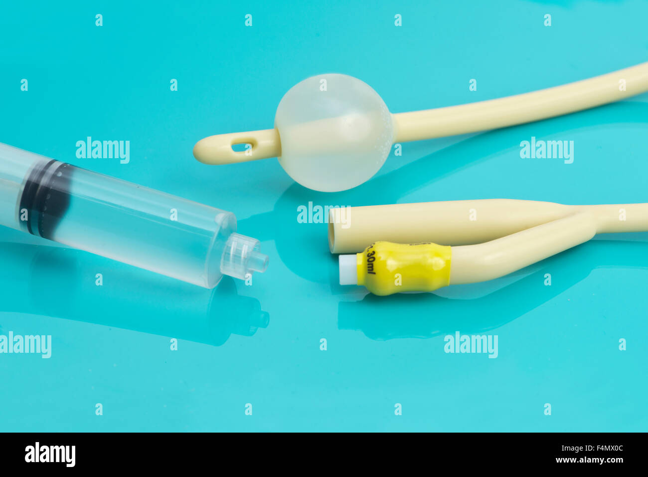 Close up of straight urinary catheter with fill syringe on aqua ...