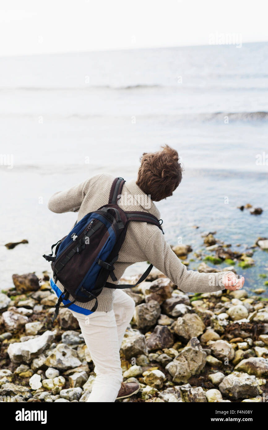 Rear view of man throwing stones in water at beach Stock Photo - Alamy