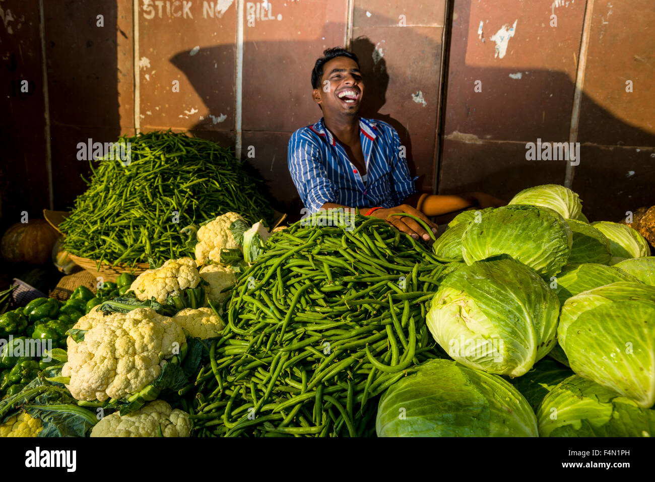 A salesman, loughing, is selling cauliflower, beans and cabbage at an ...
